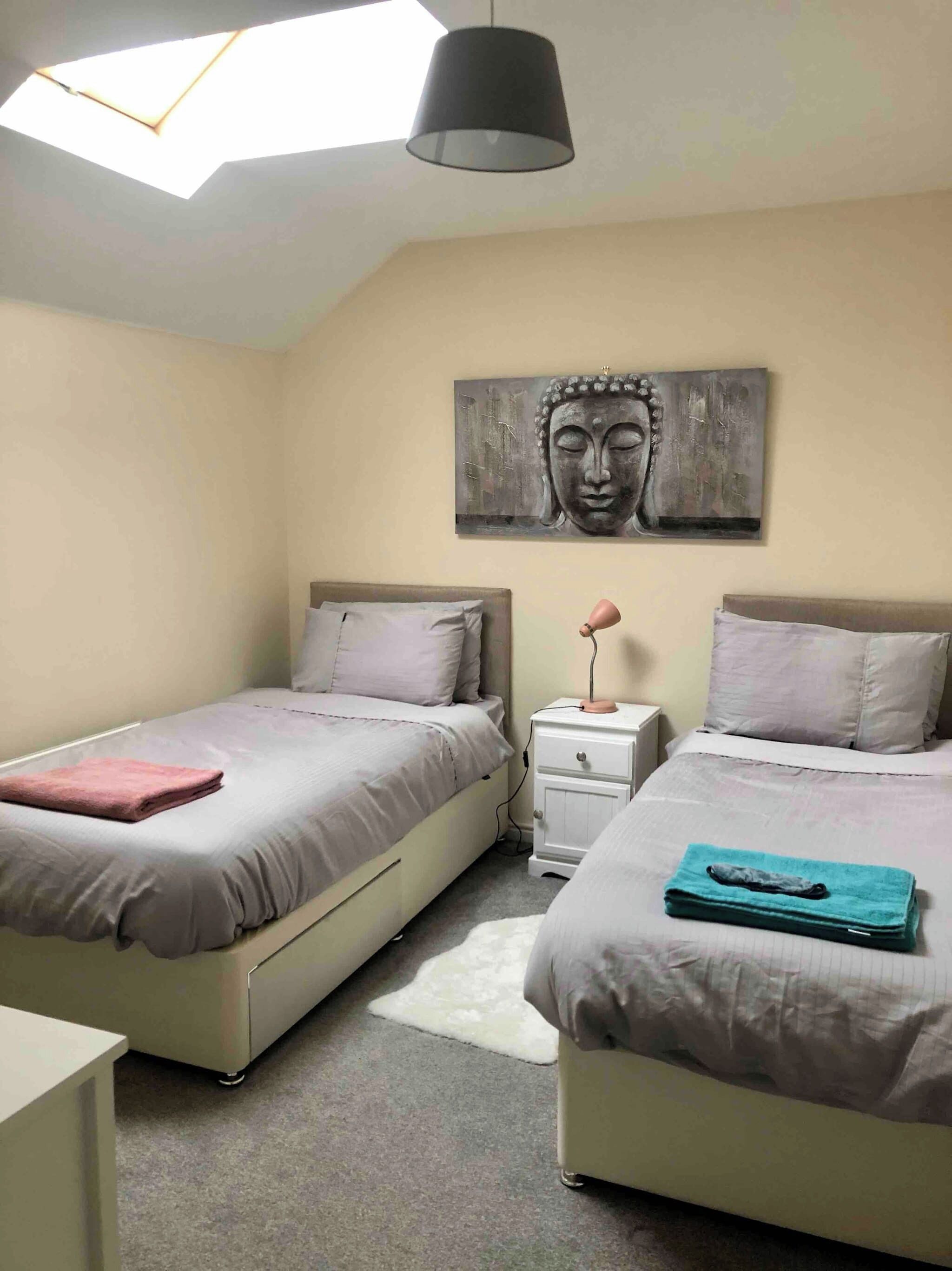 Quarto com duas camas, um claraboia, pintura de Buda e uma pequena mesa de cabeceira com abajur.