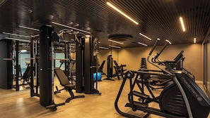 Uma academia com diversos equipamentos de exercício, incluindo um banco de musculação, um suporte para agachamento e uma máquina elíptica.
