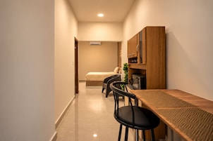 Um corredor estreito com uma cama, uma mesa de jantar com cadeiras e um espaço de cozinha compacto.