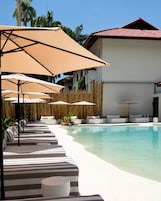 Área da piscina com espreguiçadeiras e guarda-sóis, uma piscina límpida e um edifício com telhado vermelho.