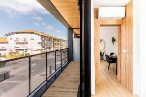 Varanda com piso de madeira e grade de metal, com vista para a rua e edifícios.