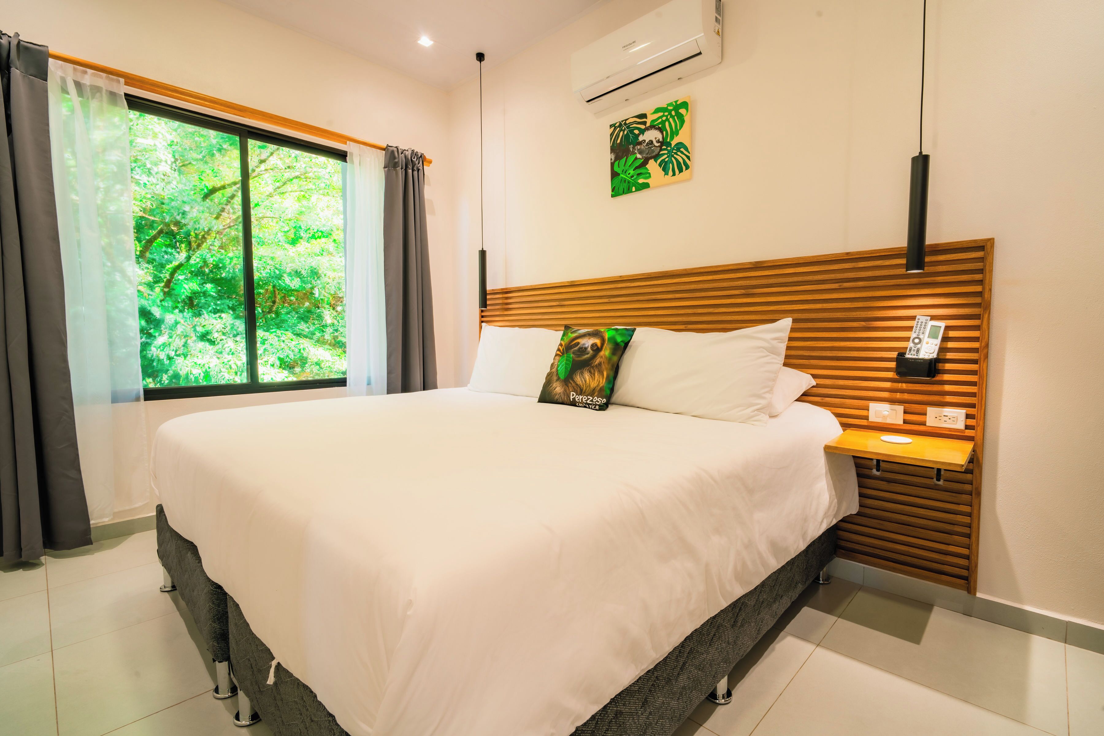 Quarto de hotel com uma cama grande, uma mesinha de cabeceira com telefone e uma janela com cortinas.