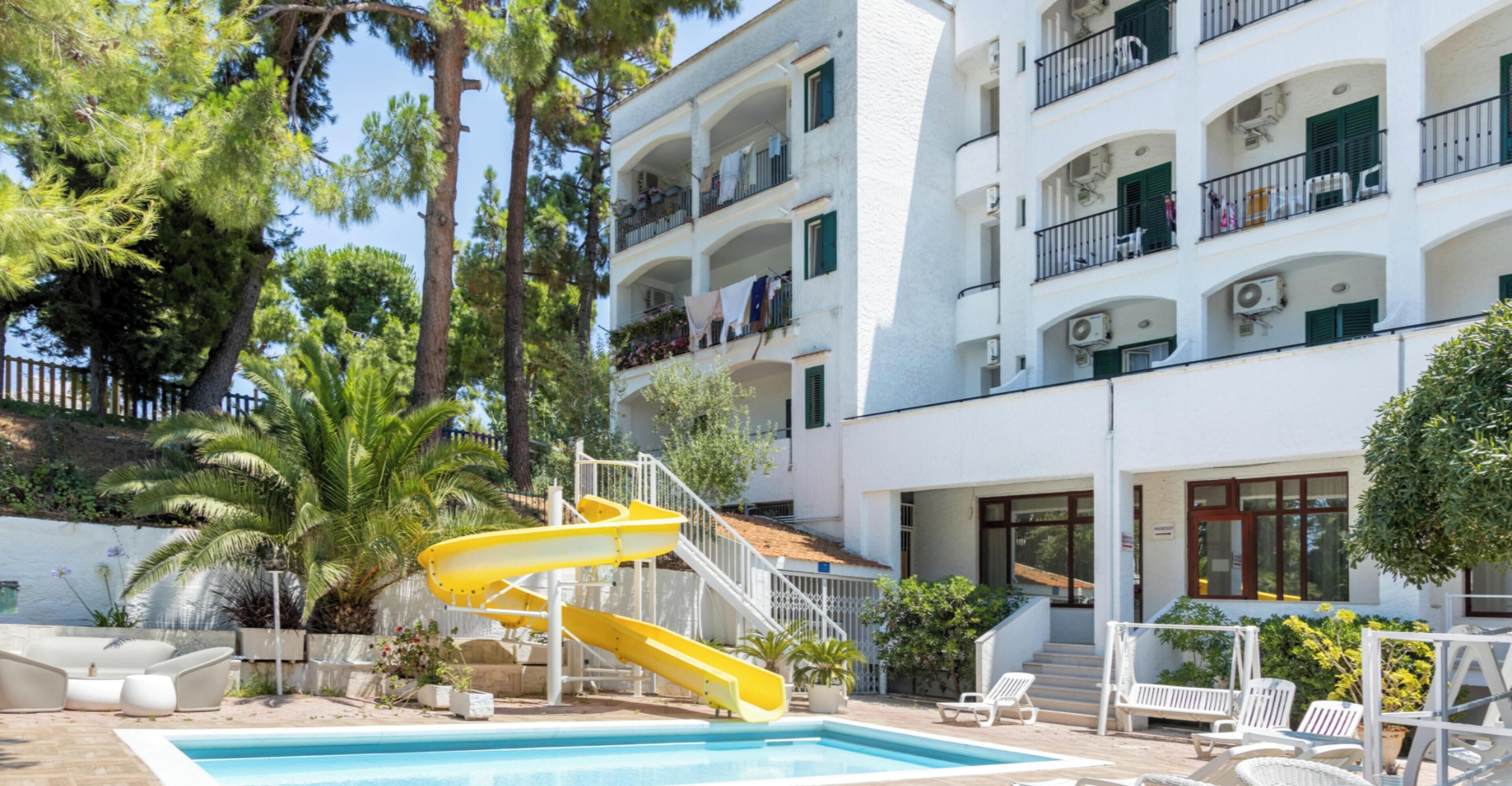 Um hotel com piscina, escorregas amarelos, área de estar externa e um edifício de vários andares com sacadas.