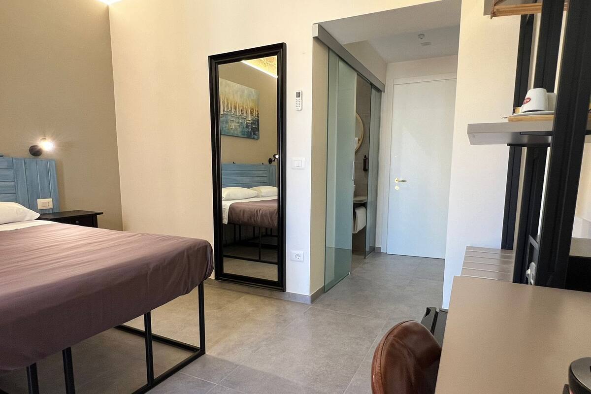 Quarto de hotel com cama, escrivaninha e uma cadeira. Há uma porta que dá para um banheiro.