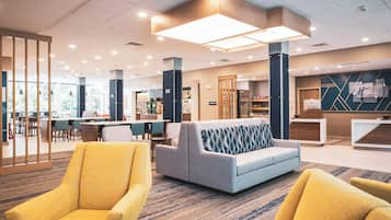 Um lobby moderno com áreas de estar, balcão de recepção e café.