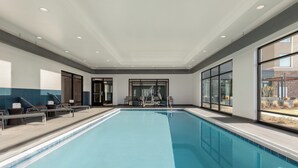 Piscina com vista para um edifício, área de estar coberta e uma porta que dá para outro espaço.
