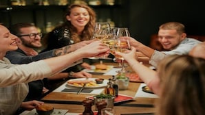 Um grupo de pessoas brindando com taças de vinho em uma mesa de restaurante.