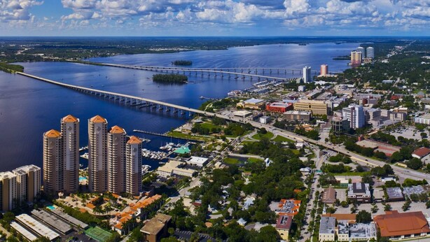 Paisagem costeira com uma ponte notável, edifícios altos e uma marina.