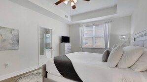 Quarto moderno com cama grande, ventoinha no teto, televisão e janela com persianas.