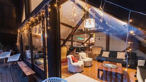 Um interior com deck de madeira, assentos acolchoados brancos e luzes de cordão.