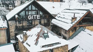 Um edifício com uma placa grande com a inscrição 'GITE', paredes de pedra e telhados cobertos de neve.