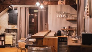 Um interior rústico com um barril de madeira, um piano, área de bar e luminária pendente.