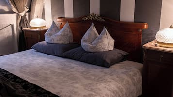 Cama bem arrumada com roupa de cama estampada em floral e almofadas decorativas, cabeceira de madeira e abajures de cada lado.