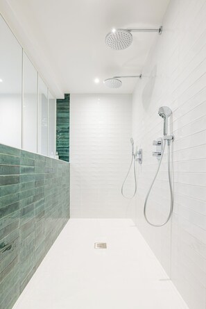 Um banheiro moderno com paredes revestidas de azulejos brancos, uma parede de destaque em verde, uma banheira branca e um chuveiro com chuveiro manual e torneira embutida.