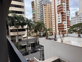 Um edifício alto com várias varandas, piscina e palmeiras ao redor.