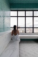 Uma pessoa sentada num banco perto de uma janela grande com vista para a cidade.
