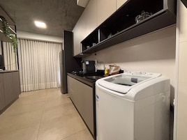 Cozinha moderna com máquina de lavar embutida, bancada preta e janela com persianas verticais.