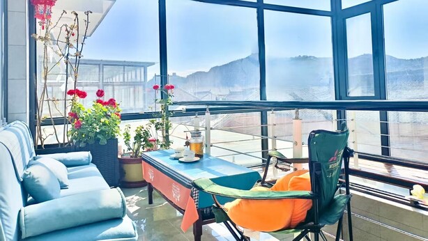 Um quarto iluminado pelo sol com vista para um corpo de água, um sofá azul, uma mesa com um bule e uma cadeira com almofada.