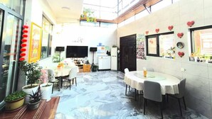 Um espaço amplo e interno com teto alto, mesa de jantar, cadeiras e plantas em vasos.
