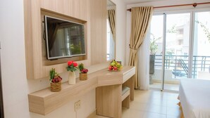 Quarto de hotel moderno com toucador de madeira, televisão de ecrã plano, área de refeições e varanda com cortinas.