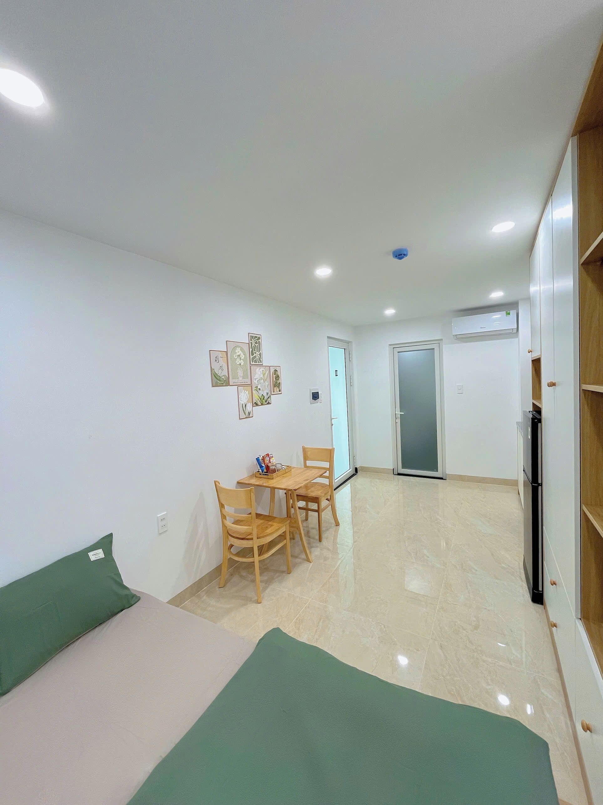 Quarto com cama, mesa de jantar com cadeiras, geladeira e aparelho de ar condicionado.