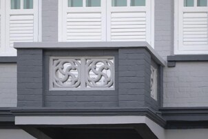 Fachada de edifício com grade decorativa na janela e contraventanas brancas.