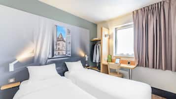 Quarto de hotel com duas camas, uma escrivaninha, um guarda-roupa e uma janela com cortinas.