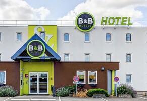 Um hotel tipo bed and breakfast com fachada amarela vibrante, logotipo azul e verde, e placa indicando que não há estacionamento.