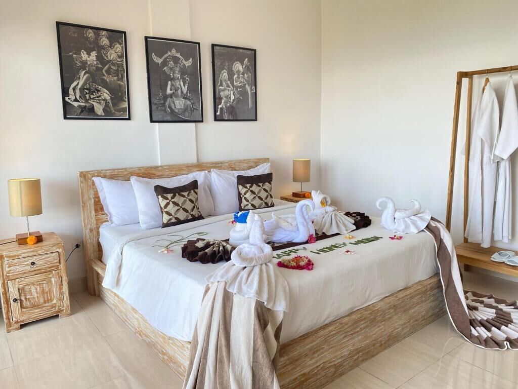 Cama bem arrumada com colcha branca e marrom estampada, duas obras de arte preto e branco penduradas na parede, mesa de cabeceira de madeira com abajur e porta-toalhas de madeira com toalhas brancas.