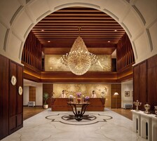 Um hall imponente com teto alto, um grande lustre e uma recepção com painel decorativo.