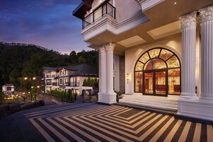 Uma entrada imponente de hotel, com uma grande porta em arco, colunas e uma alameda bem iluminada que leva à entrada.