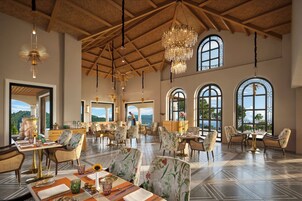 Uma ampla sala de jantar com pé direito alto, grandes janelas e lustres elegantes.