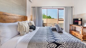 Quarto de hotel moderno com uma cama grande, cabeceira de madeira, televisão e varanda com vista para a cidade.
