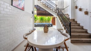 Um interior moderno com uma parede de tijolos brancos, uma mesa redonda com cadeiras, uma escada com degraus de madeira e uma cesta suspensa.