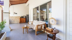 Um pátio amplo com um sofá de madeira, uma mesa pequena e um ventilador decorativo.