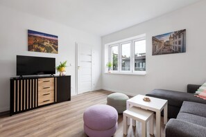 Uma sala de estar moderna com uma TV de tela plana, um sofá, pufes, uma mesinha e duas pinturas na parede.