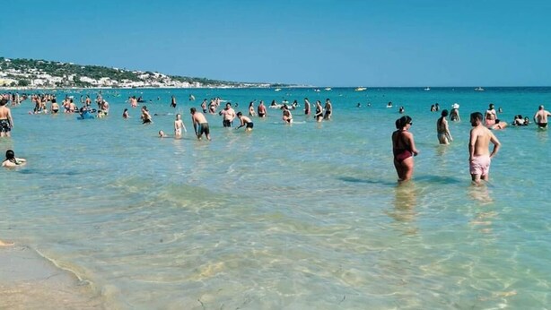 Uma praia movimentada com pessoas nadando e caminhando na água.