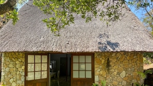 Uma casa de campo com telhado de palha, paredes de pedra, portas de madeira e um pequeno alpendre.