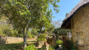Uma casa de pedra com telhado de palha, rodeada por um jardim com diversas plantas e um muro de pedra.
