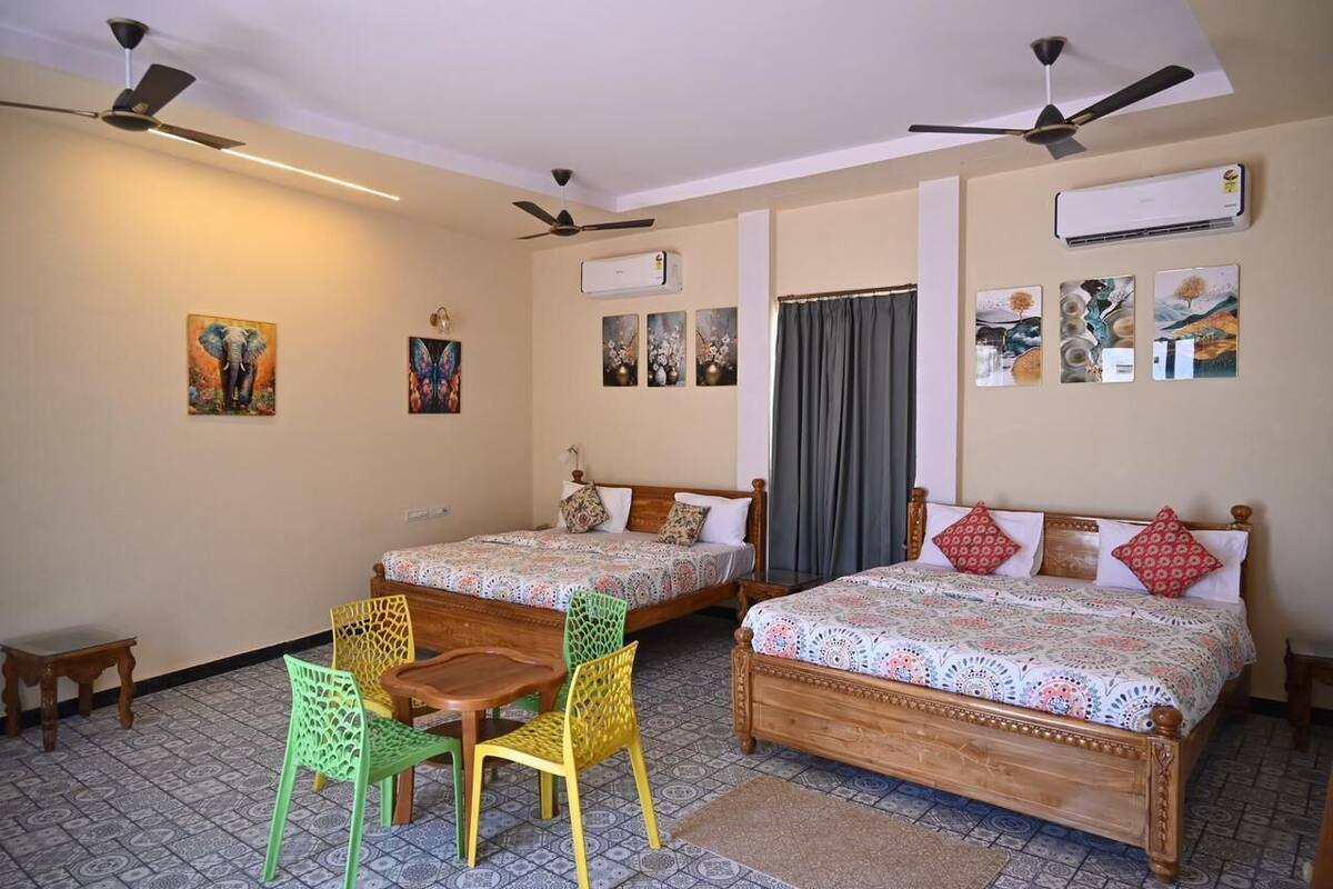 Quarto com duas camas, uma mesa de jantar, cadeiras, ventiladores de teto e obras de arte nas paredes.