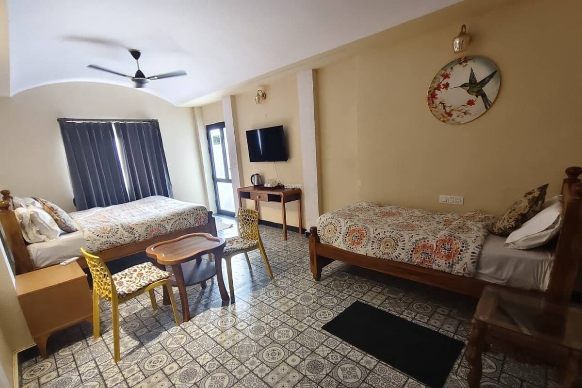 Quarto com duas camas, uma escrivaninha, uma cadeira, uma televisão e piso com ladrilhos estampados.