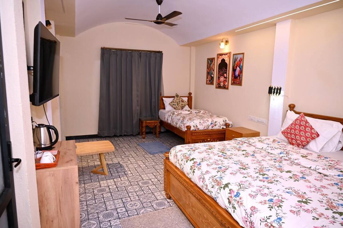 Quarto com cama, escrivaninha, cadeira, televisão e ventoinha no teto.