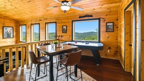 Uma cabana de madeira com mesa de bilhar, cadeiras e um ventilador de teto.