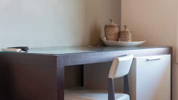 Uma secretária moderna com tampo de vidro, uma cadeira branca e objetos decorativos ao lado.