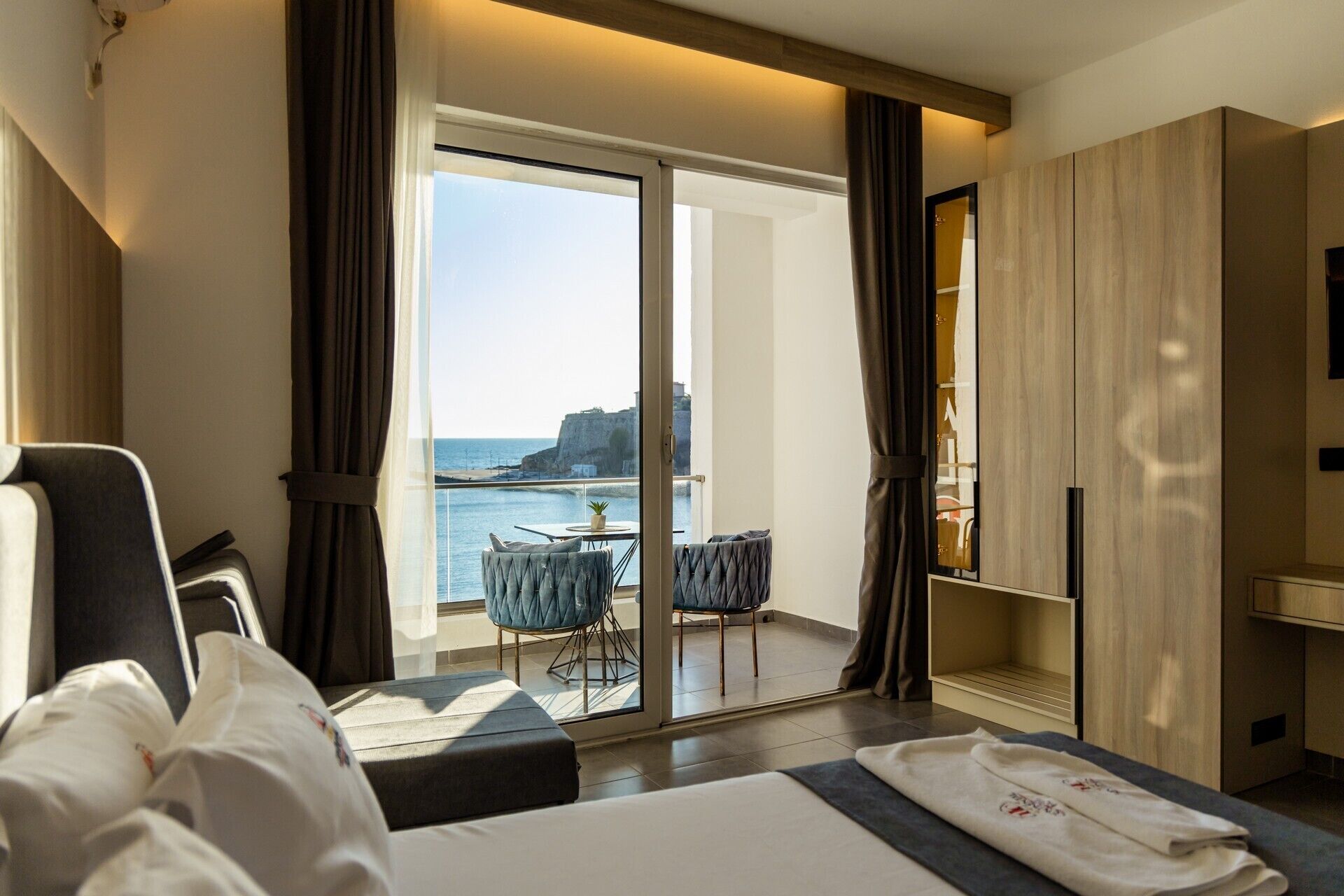 Quarto de hotel com cama, uma mesinha, uma cadeira e vista para o mar.