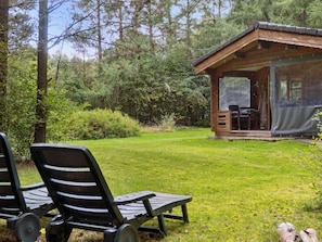 Uma cabana de madeira com varanda protegida por tela, cercada por um gramado e árvores densas.