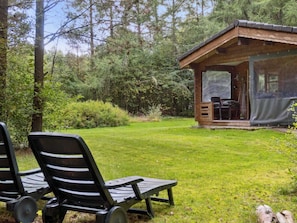 Uma cabana de madeira com varanda coberta, cercada por gramado e árvores densas.