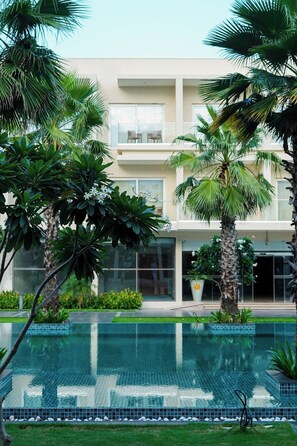 Um hotel moderno com piscina, vegetação exuberante e um edifício de dois andares com grandes janelas.