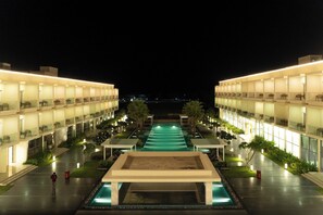 Um hotel com piscina central, várias varandas e área externa bem iluminada.