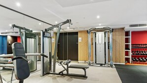Uma academia com diversos equipamentos de exercícios, um espelho e um suporte com halteres.